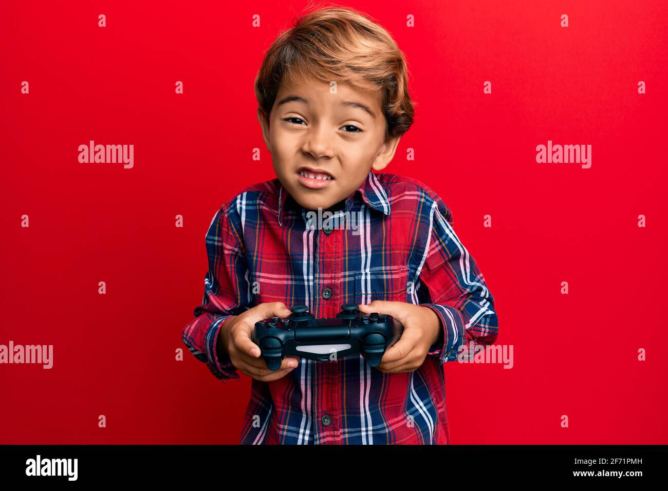 Adorable latin kid playing video game holding controller clueless and ...