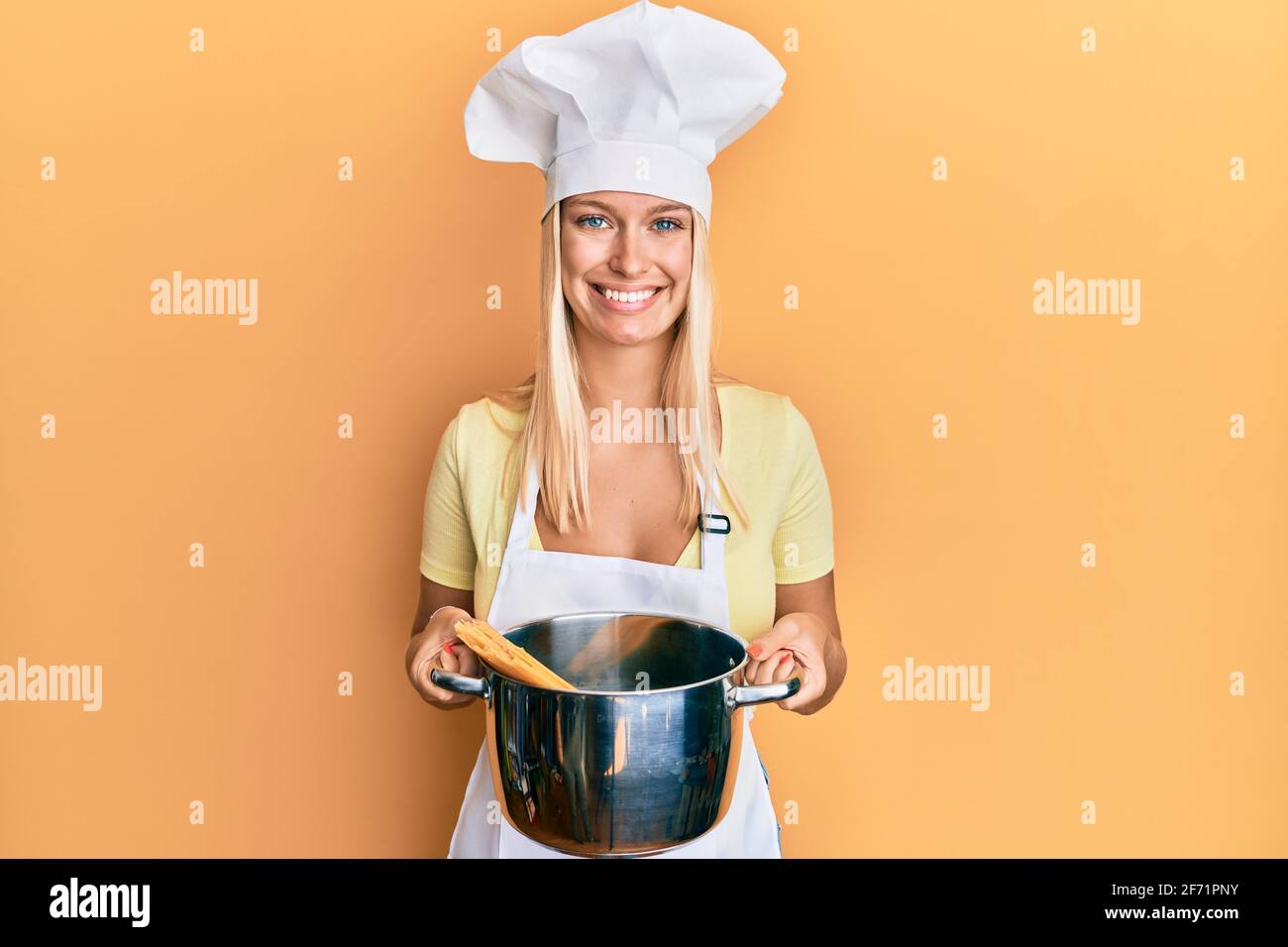 Young blonde girl cooking spaghetti smiling with a happy and cool smile ...
