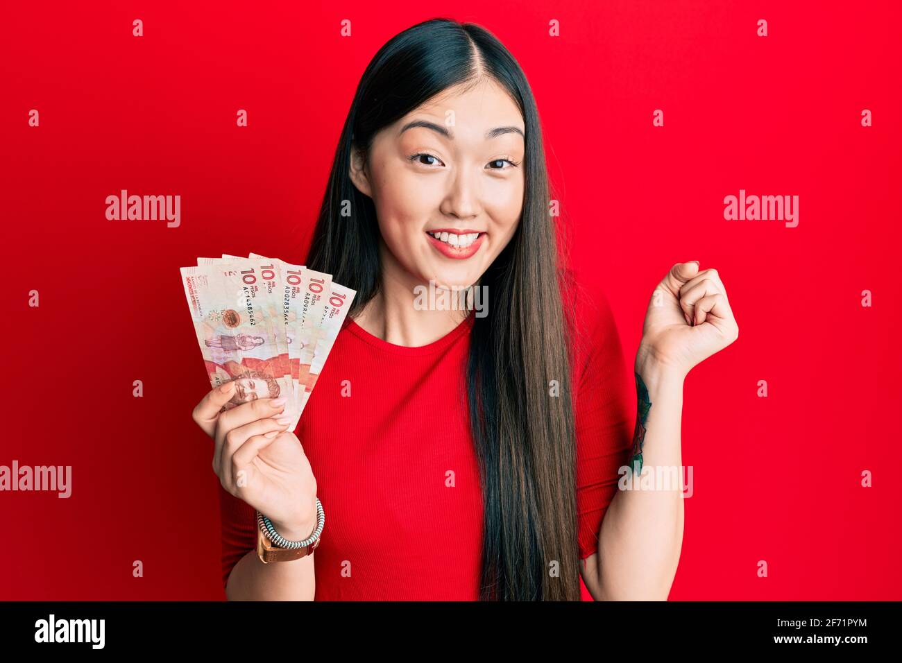 Young chinese woman holding 10 colombian pesos banknotes screaming ...