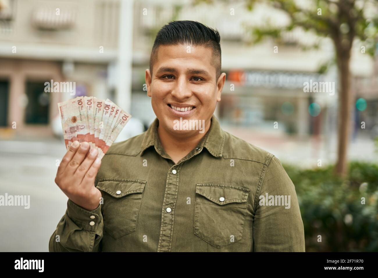 Young latin man smiling happy holding colombian pesos at the city Stock ...