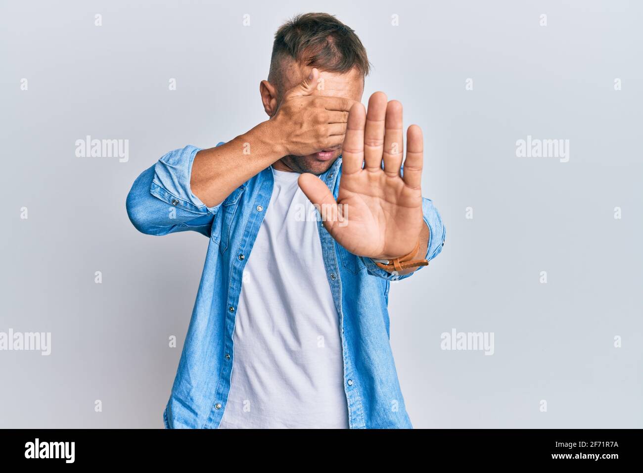 Handsome muscle man wearing casual denim jacket covering eyes with ...