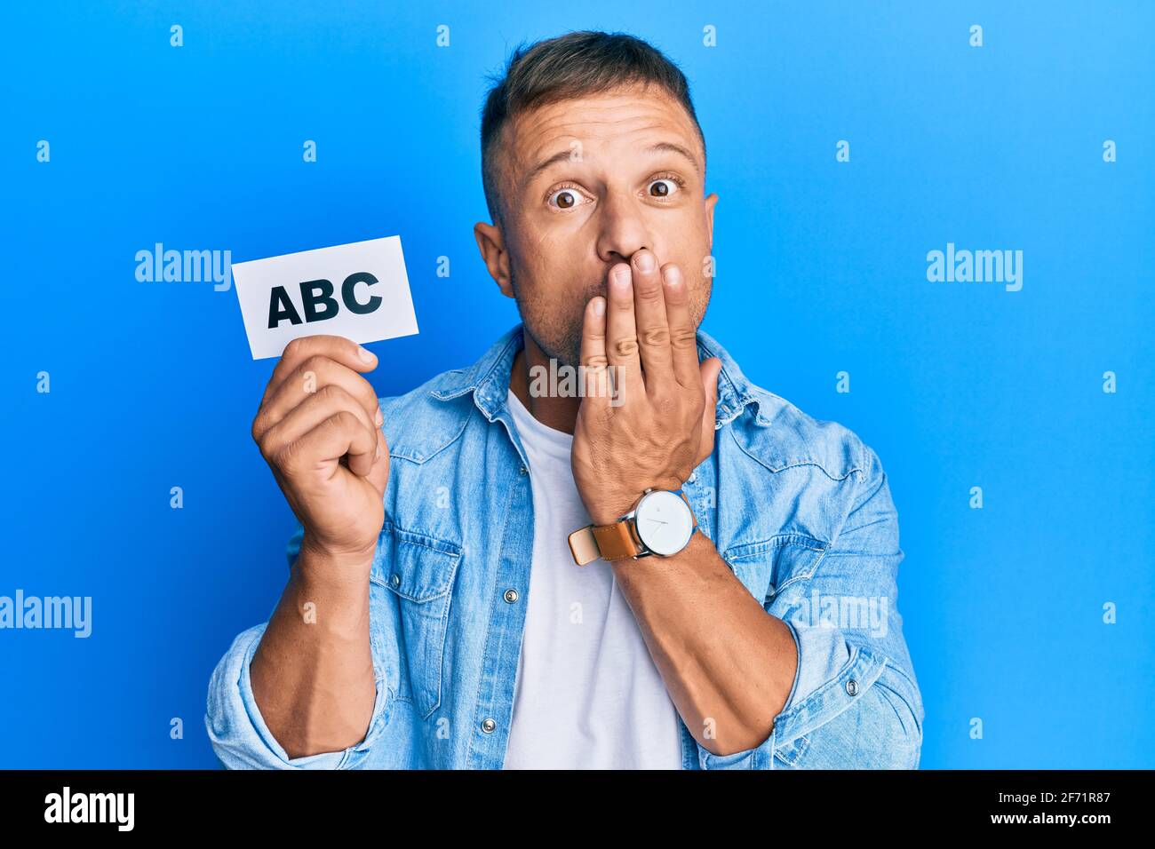 Handsome muscle man holding abc letters on paper covering mouth with ...