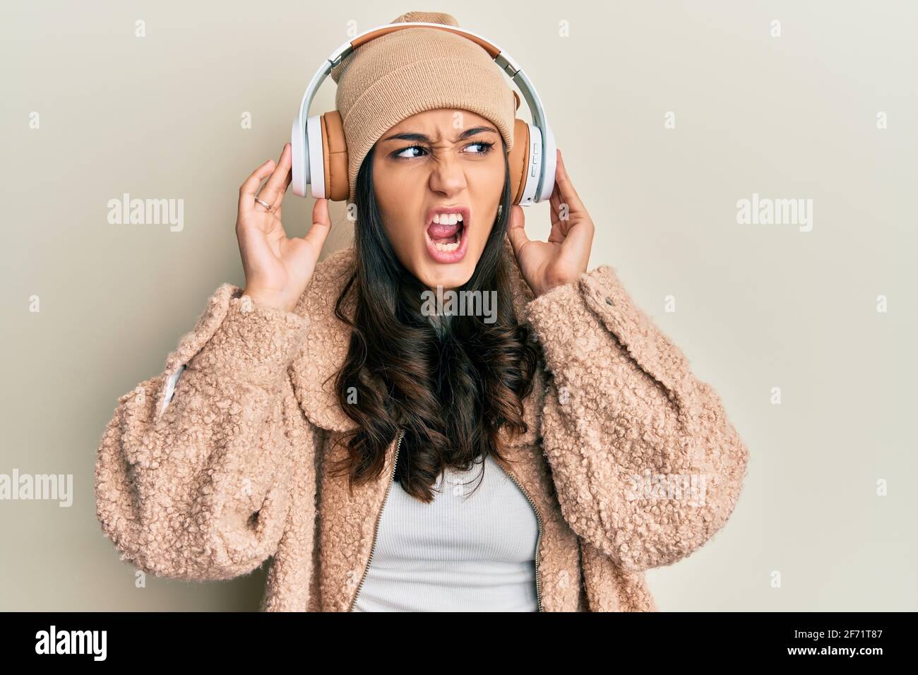 Young hispanic woman listening to music using headphones angry and mad ...
