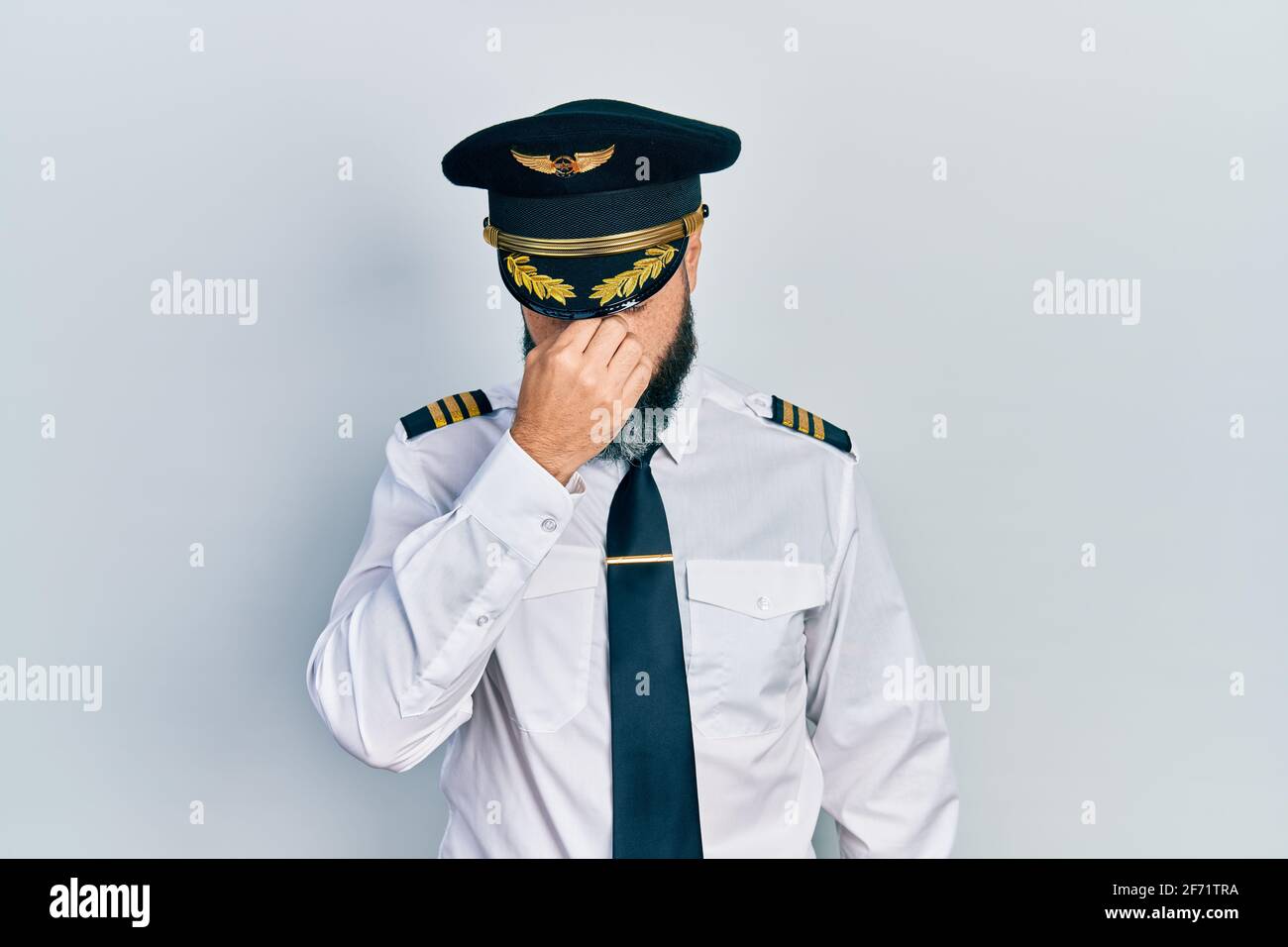 Young hispanic man wearing airplane pilot uniform tired rubbing nose ...