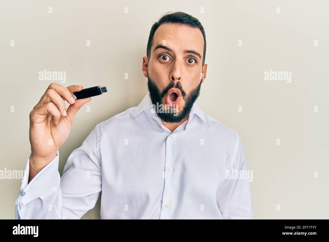 Young man with beard holding removable memory usb scared and amazed ...