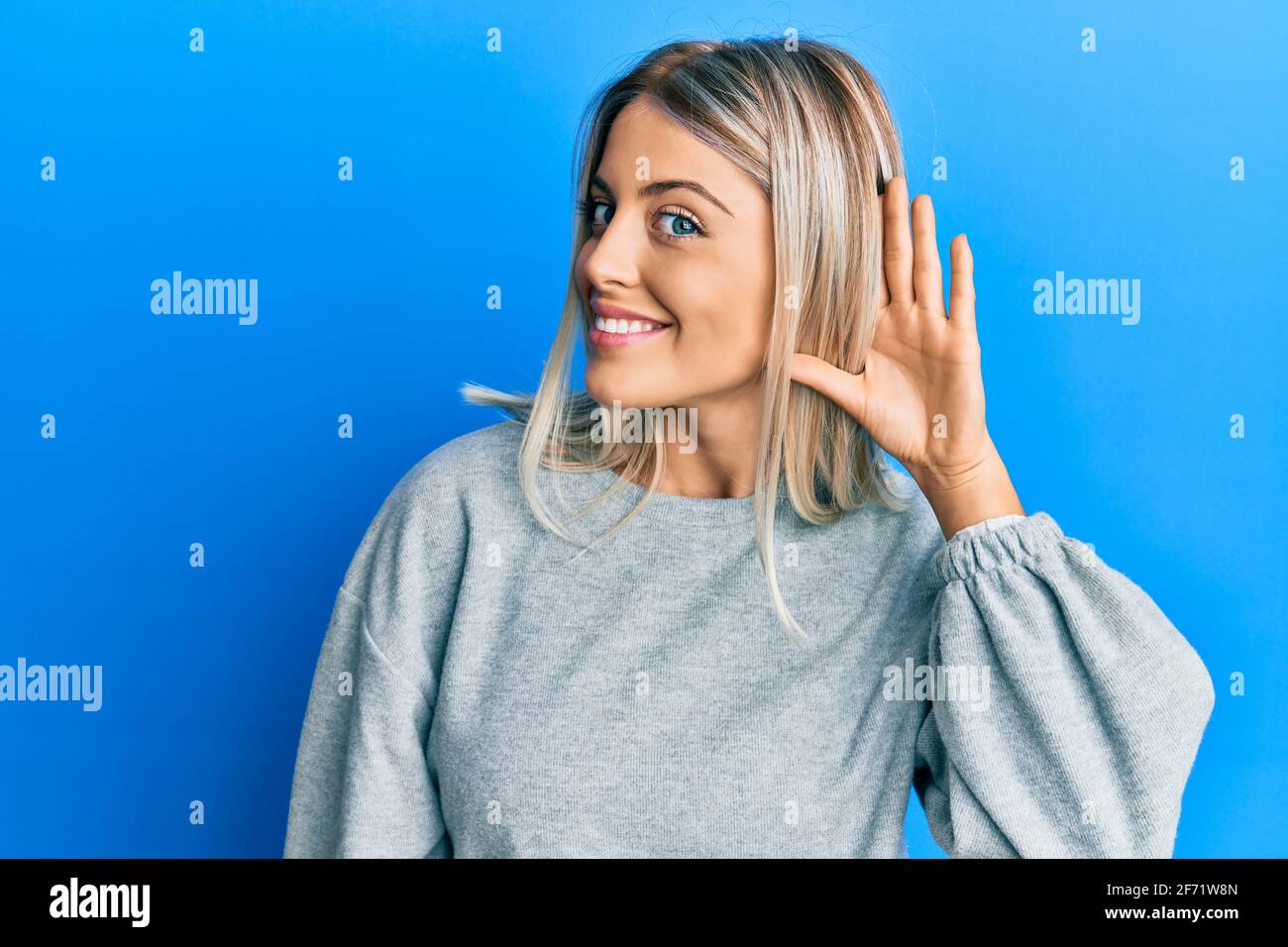 Beautiful blonde woman wearing casual clothes smiling with hand over ...