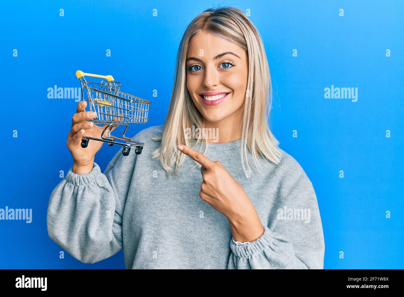 Beautiful blonde woman holding small supermarket shopping cart smiling ...