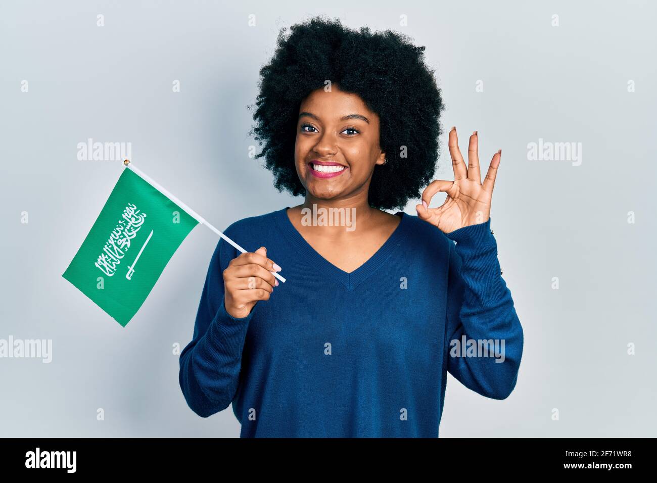 Young african american woman holding kingdom of saudi arabia flag doing ...