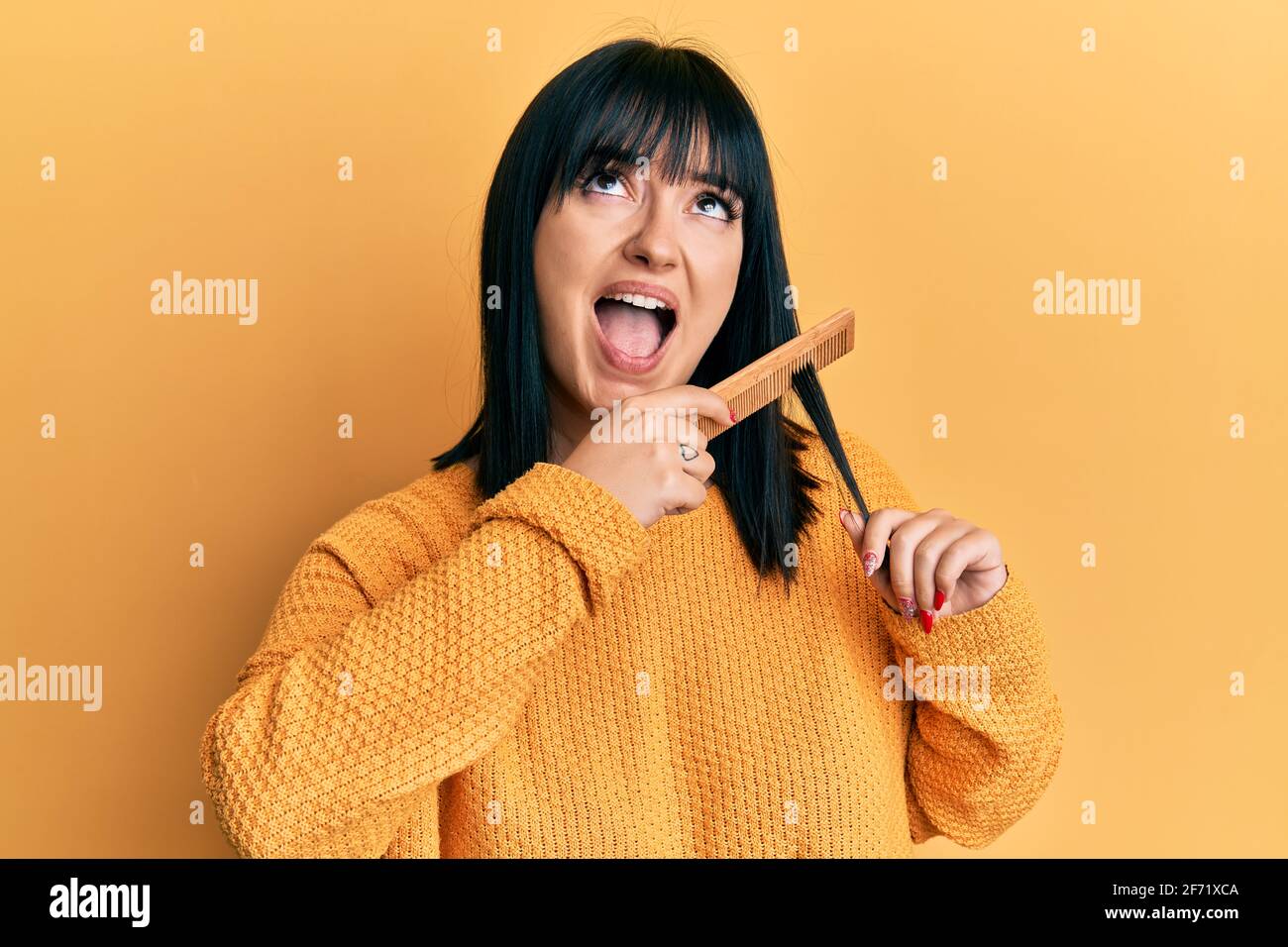 Young hispanic woman styling hair using comb angry and mad screaming frustrated and furious ...