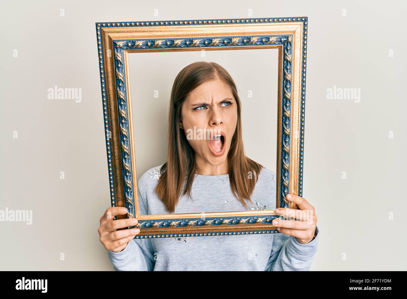 Beautiful caucasian woman holding empty frame angry and mad screaming ...