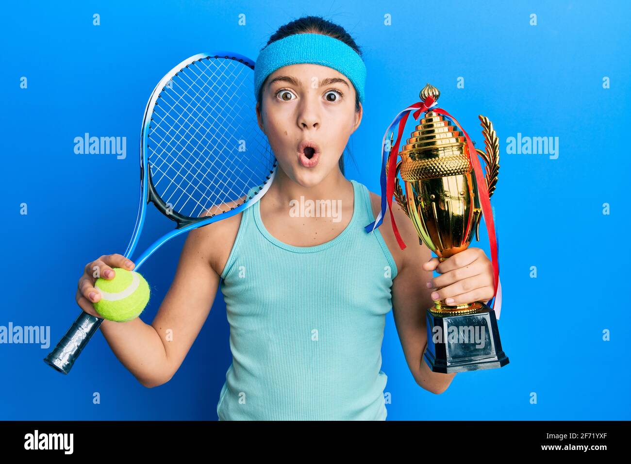 Beautiful brunette little girl playing tennis holding trophy afraid and ...