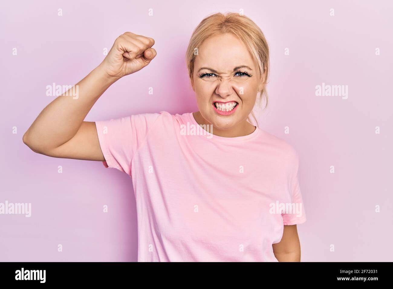 Young blonde woman wearing casual pink t shirt angry and mad raising ...
