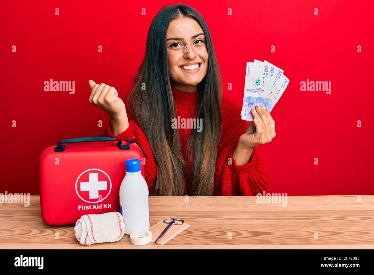 Beautiful hispanic woman with first aid kit holding colombian pesos ...