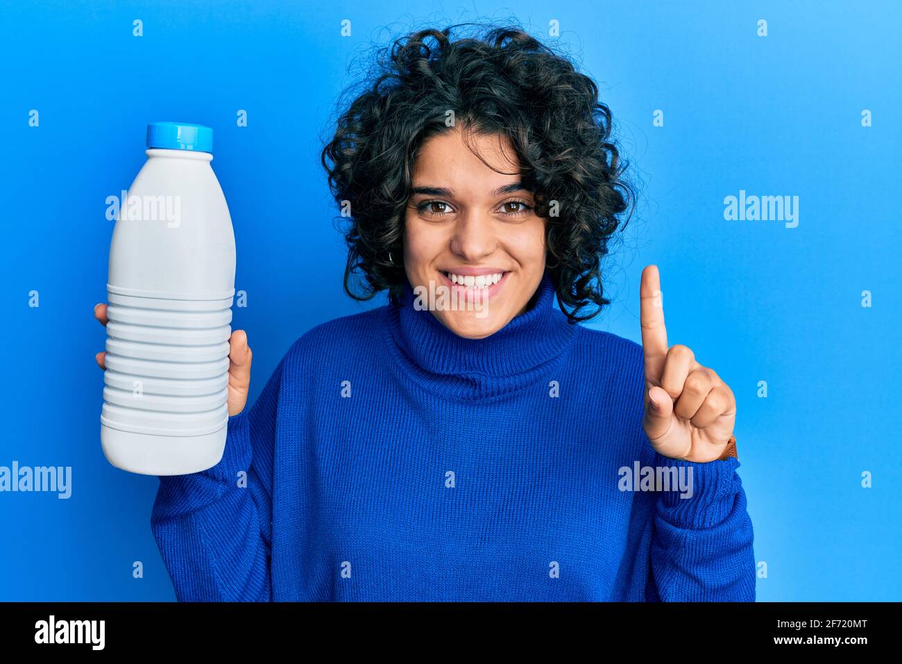 Young hispanic woman with curly hair holding liter bottle of milk ...