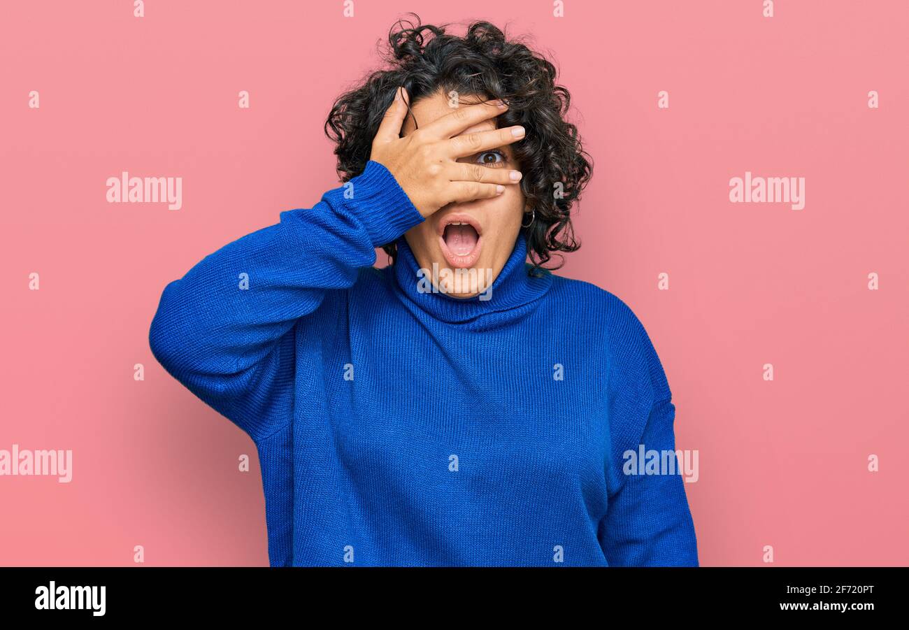 Young hispanic woman with curly hair wearing turtleneck sweater peeking ...