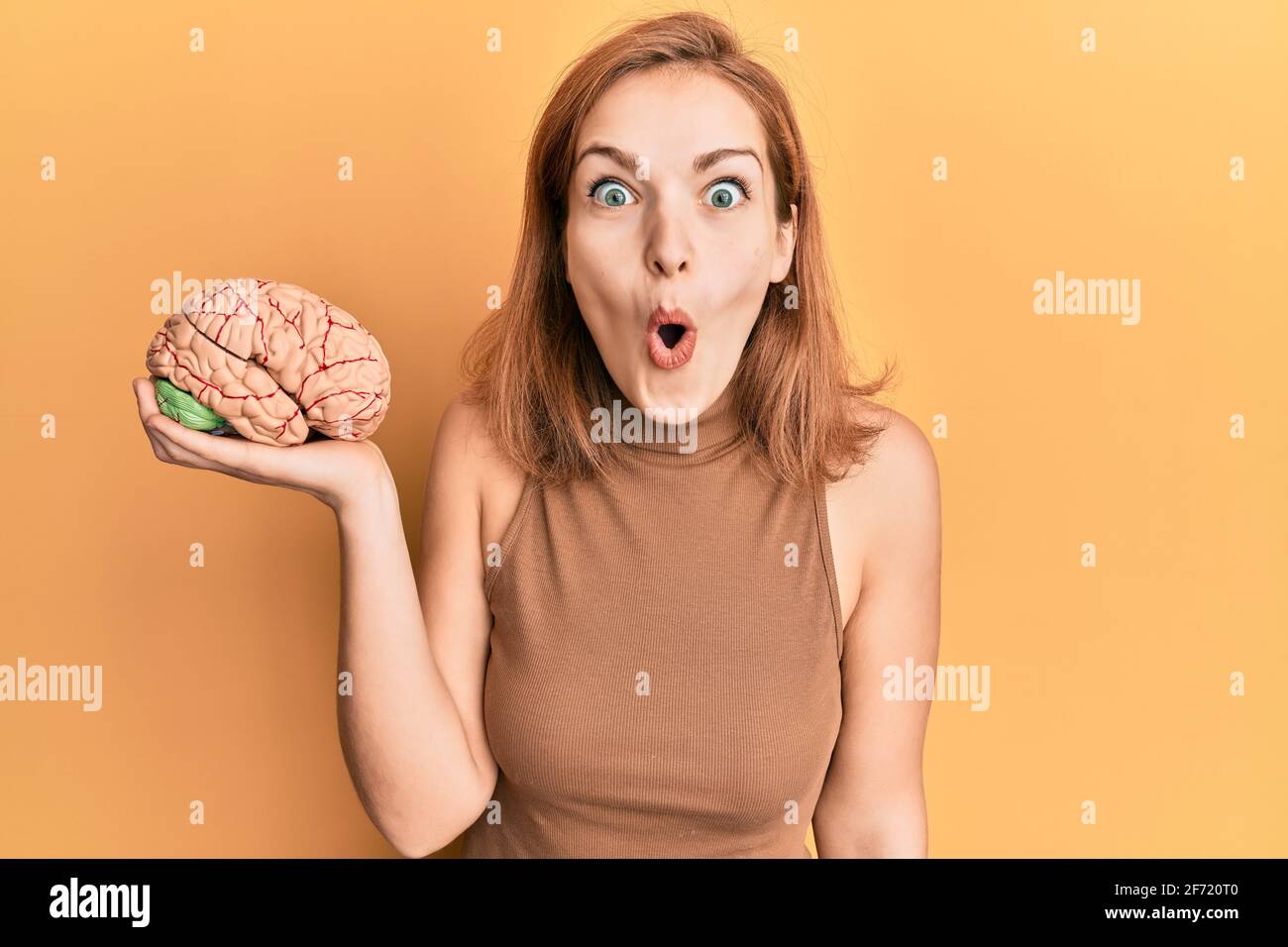 Young caucasian woman holding brain scared and amazed with open mouth ...