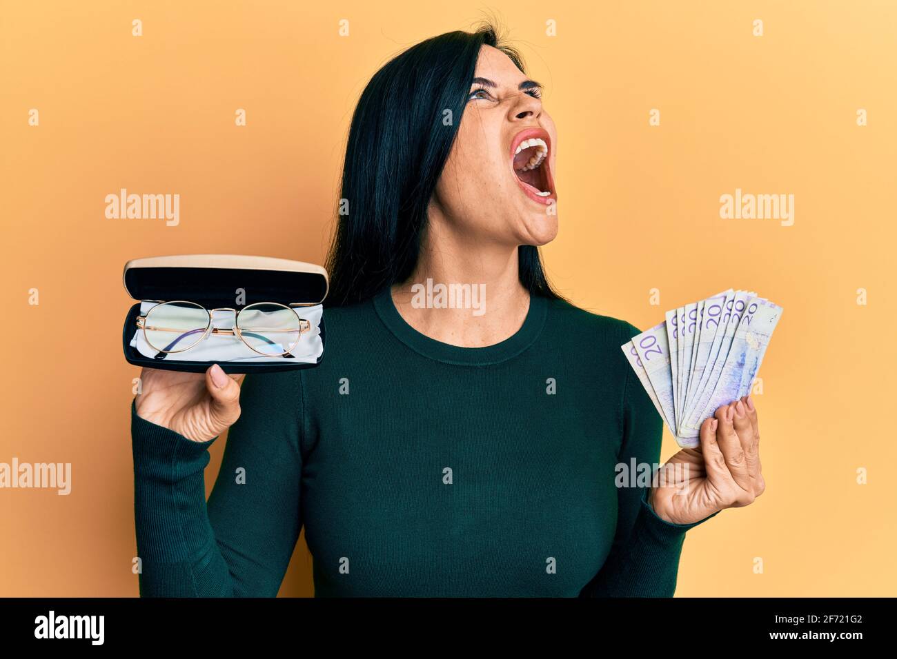 Young caucasian woman holding glasses and swedish krona banknotes angry ...