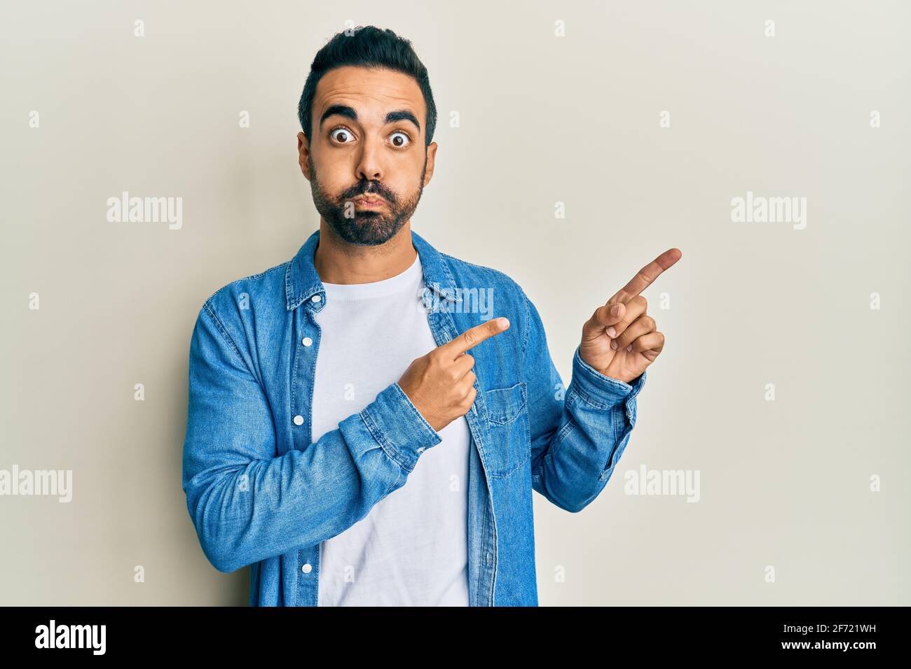 Young hispanic man pointing with fingers to himself puffing cheeks with ...