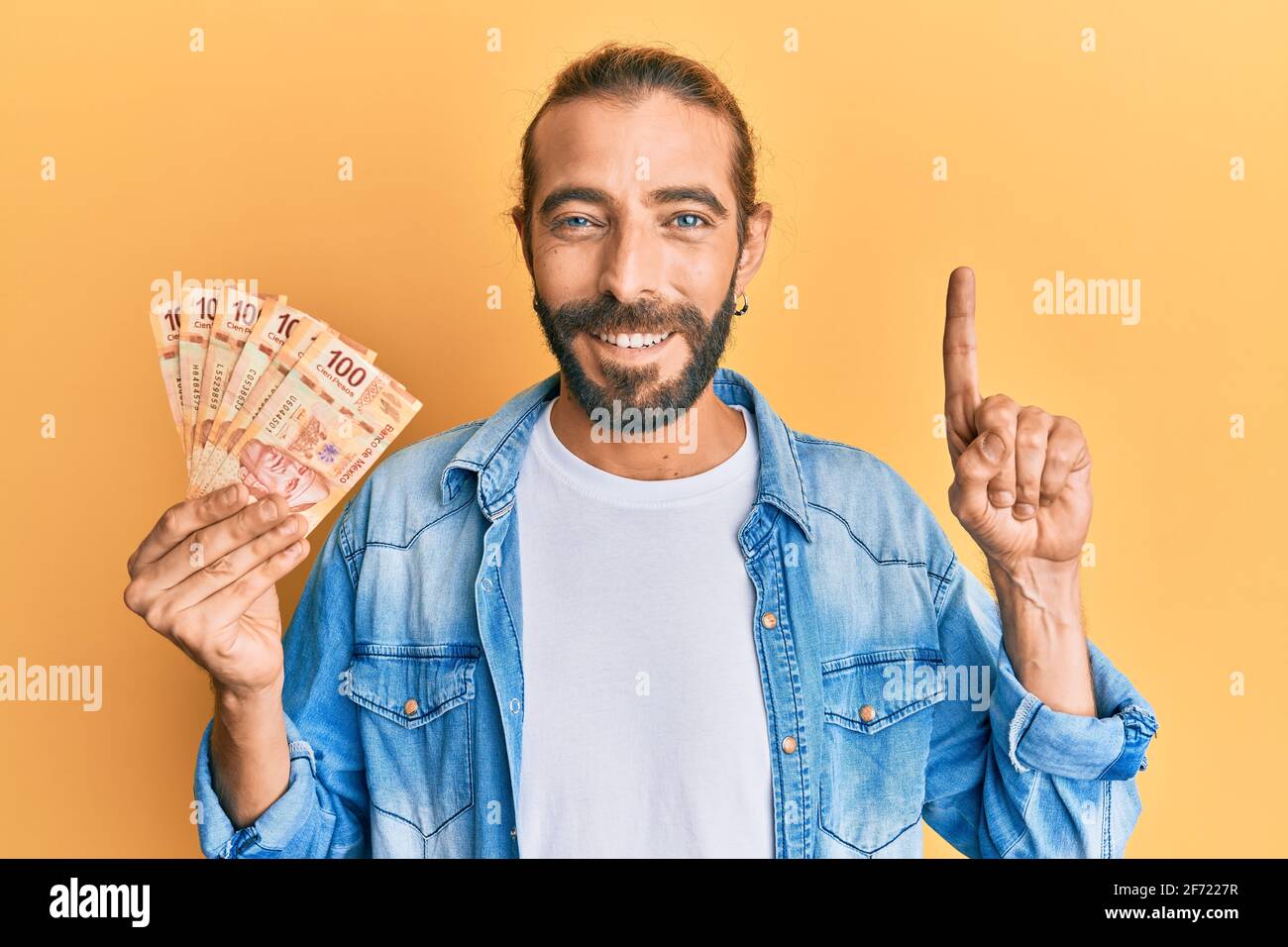 Attractive man with long hair and beard holding 100 mexican pesos ...