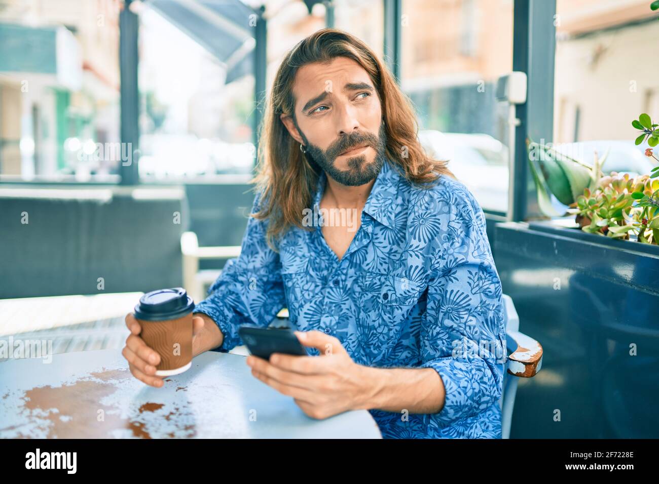 Young middle eastern man with sad face using smartphone and drinking ...