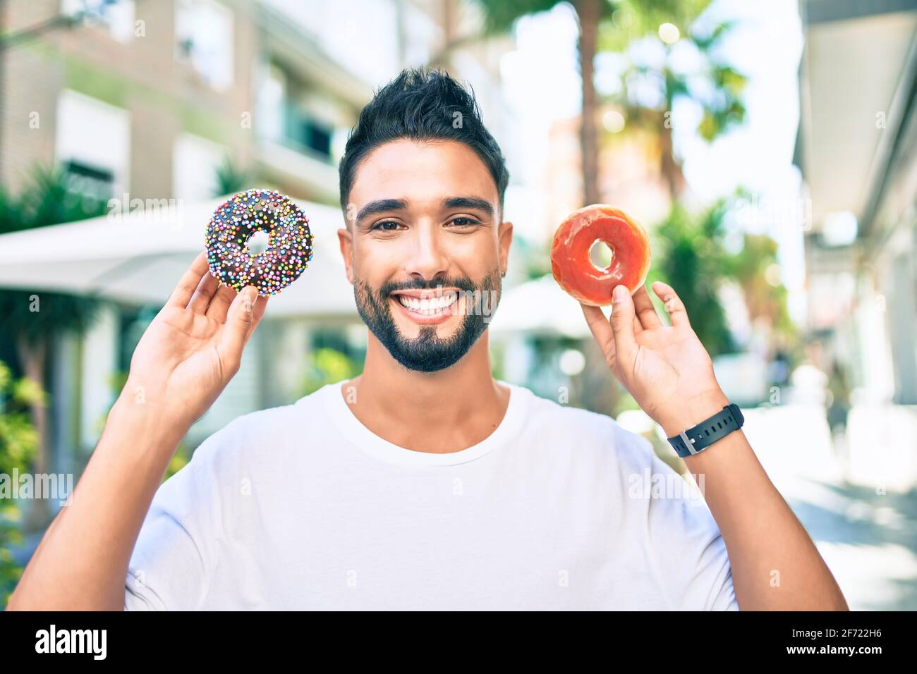 Young arab man smiling happy holding chocolate and glazed donuts at the ...