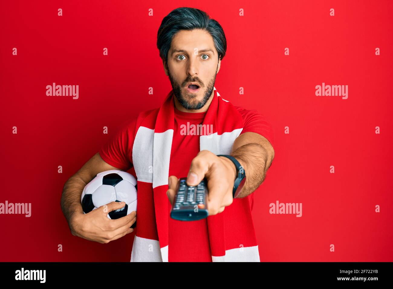 Young hispanic man football hooligan holding ball using tv control ...