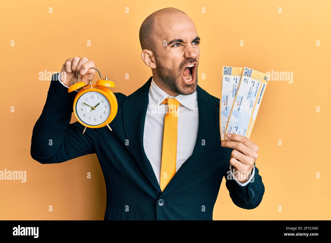 Young hispanic business man holding boarding pass and alarm clock angry ...