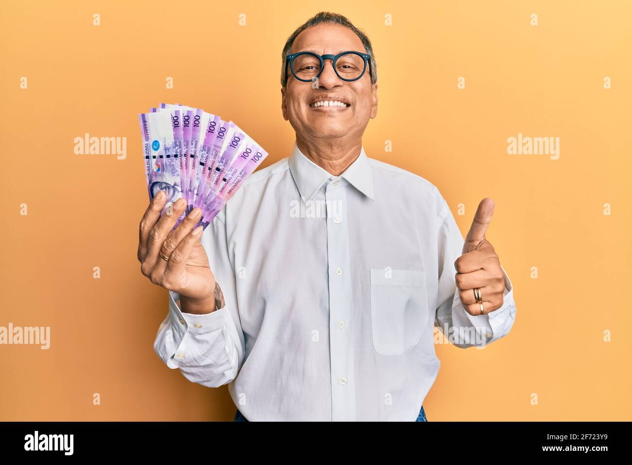 Middle age indian man holding 100 philippine peso banknotes smiling ...