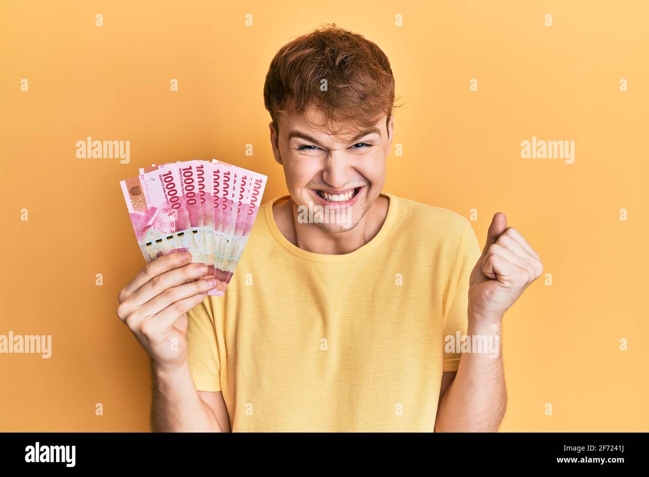 Young caucasian man holding 100000 indonesian rupiah screaming proud ...