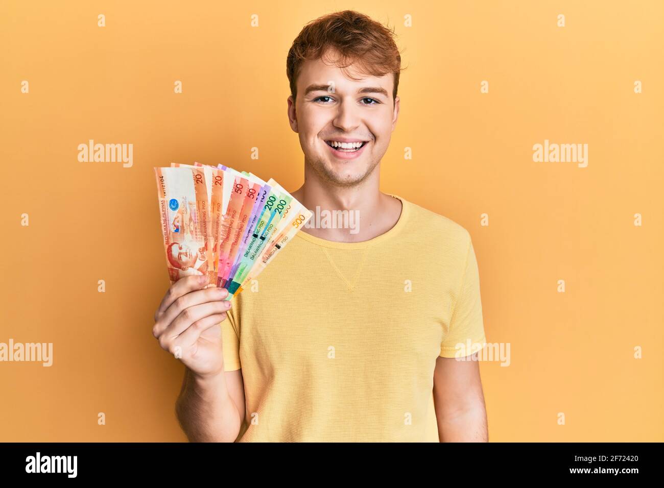 Young caucasian man holding philippine peso banknotes looking positive ...
