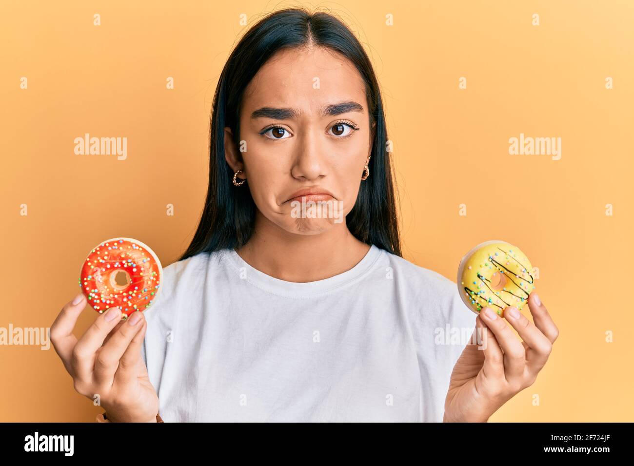 Young asian woman holding tasty colorful doughnuts depressed and worry ...