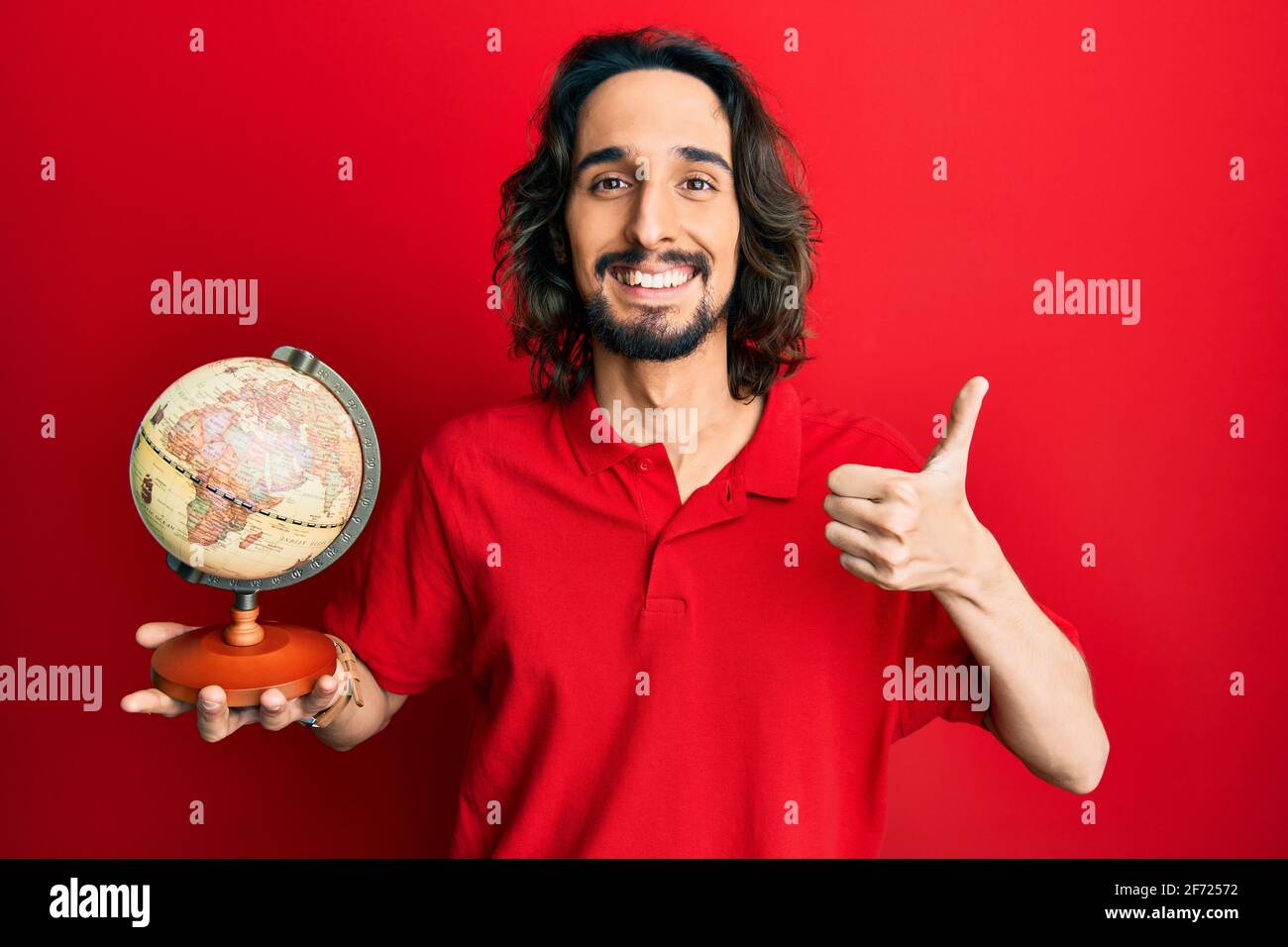 Young hispanic man holding small world ball smiling happy and positive ...