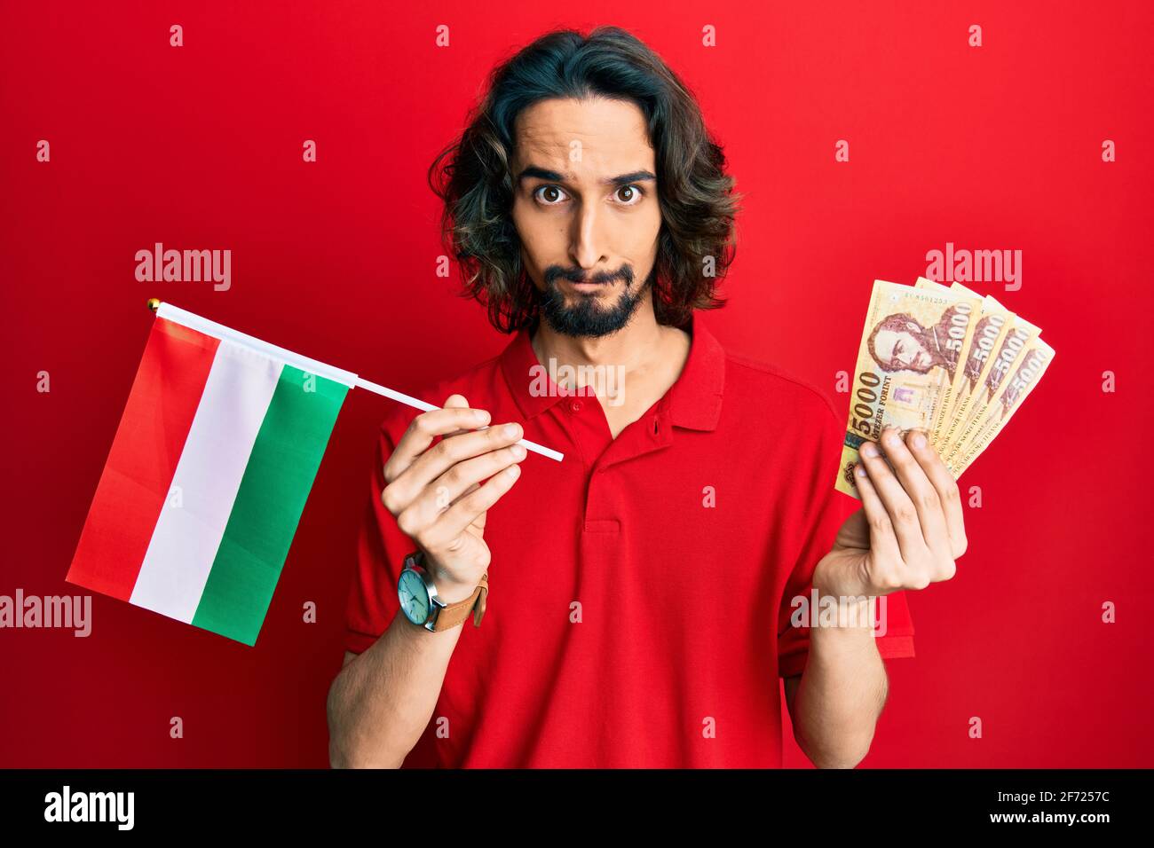 Young hispanic man holding hungary flag and forints depressed and worry ...