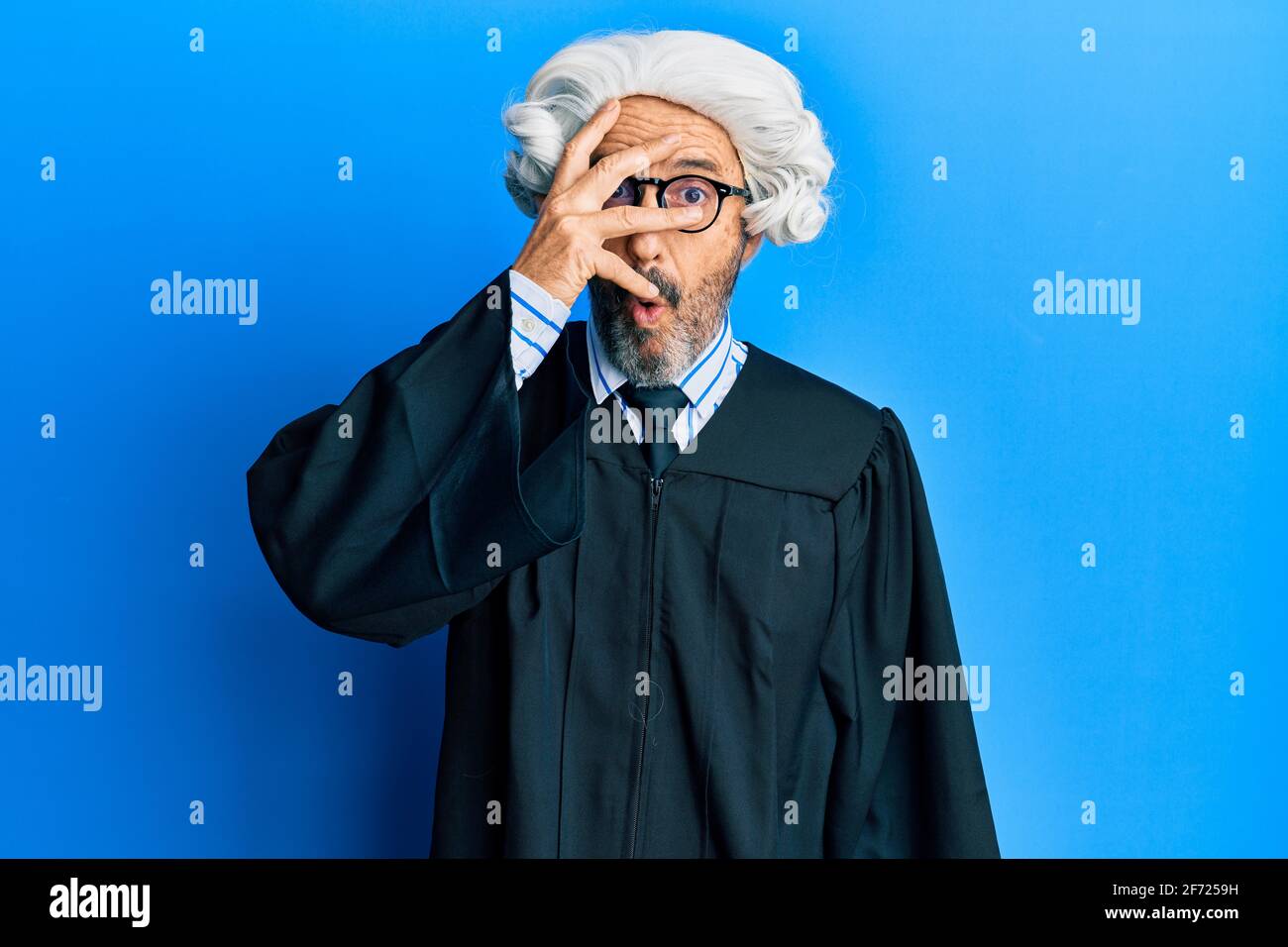 Middle age hispanic man wearing judge uniform peeking in shock covering ...