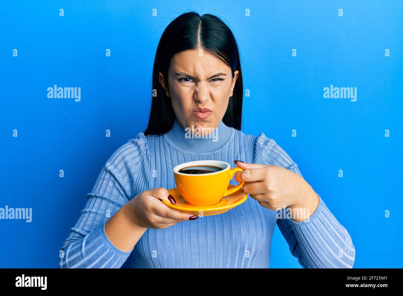 Beautiful brunette woman drinking a yellow cup of black coffee skeptic ...