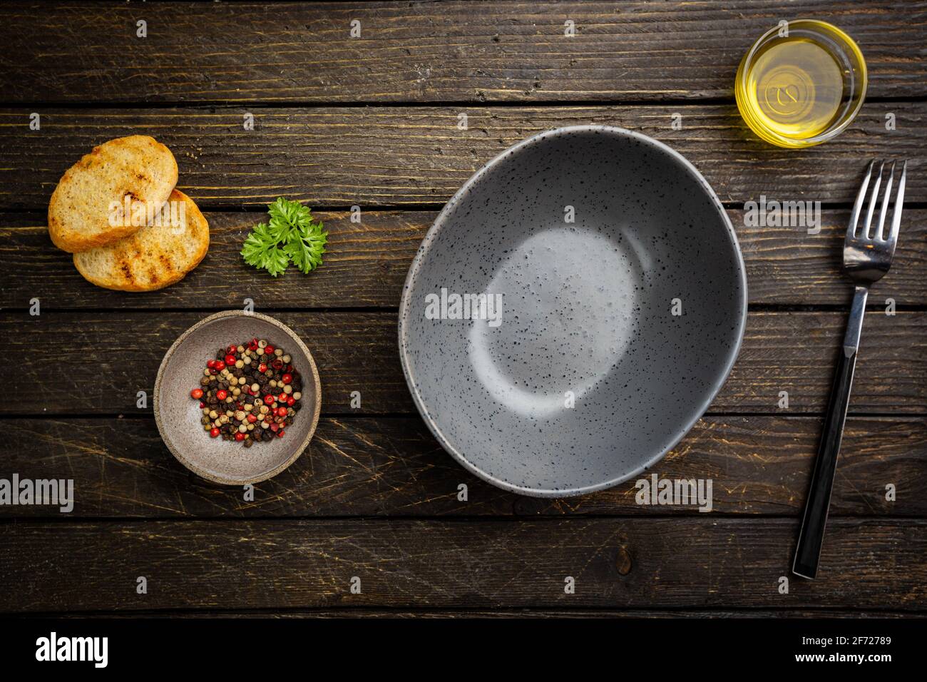 Empty plate for salad, condiments and spices on wooden kitchen table ...