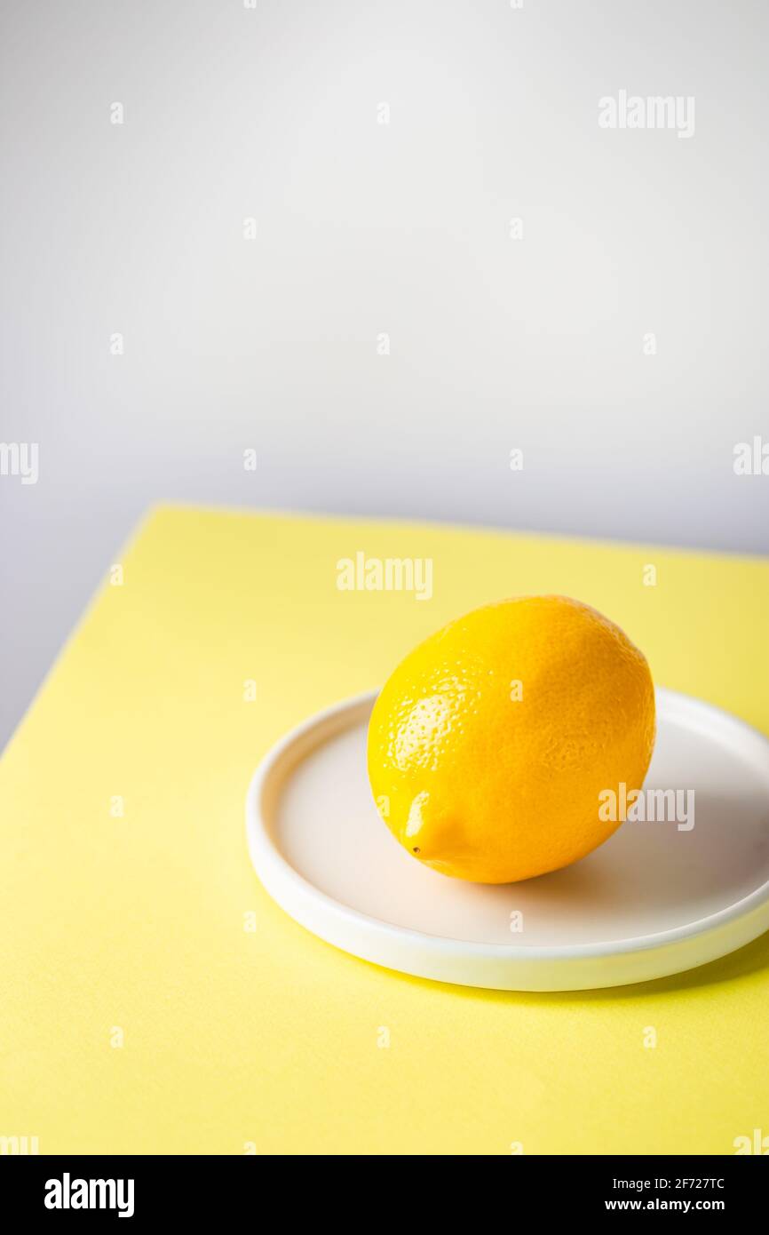 Fresh lemon on plate over two tone background, yellow and white ...