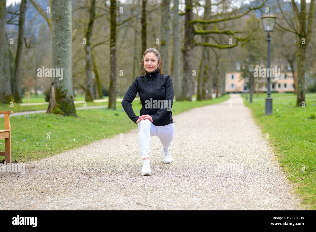 Middle-aged woman limbering up doing stretch and lunge exercises before ...