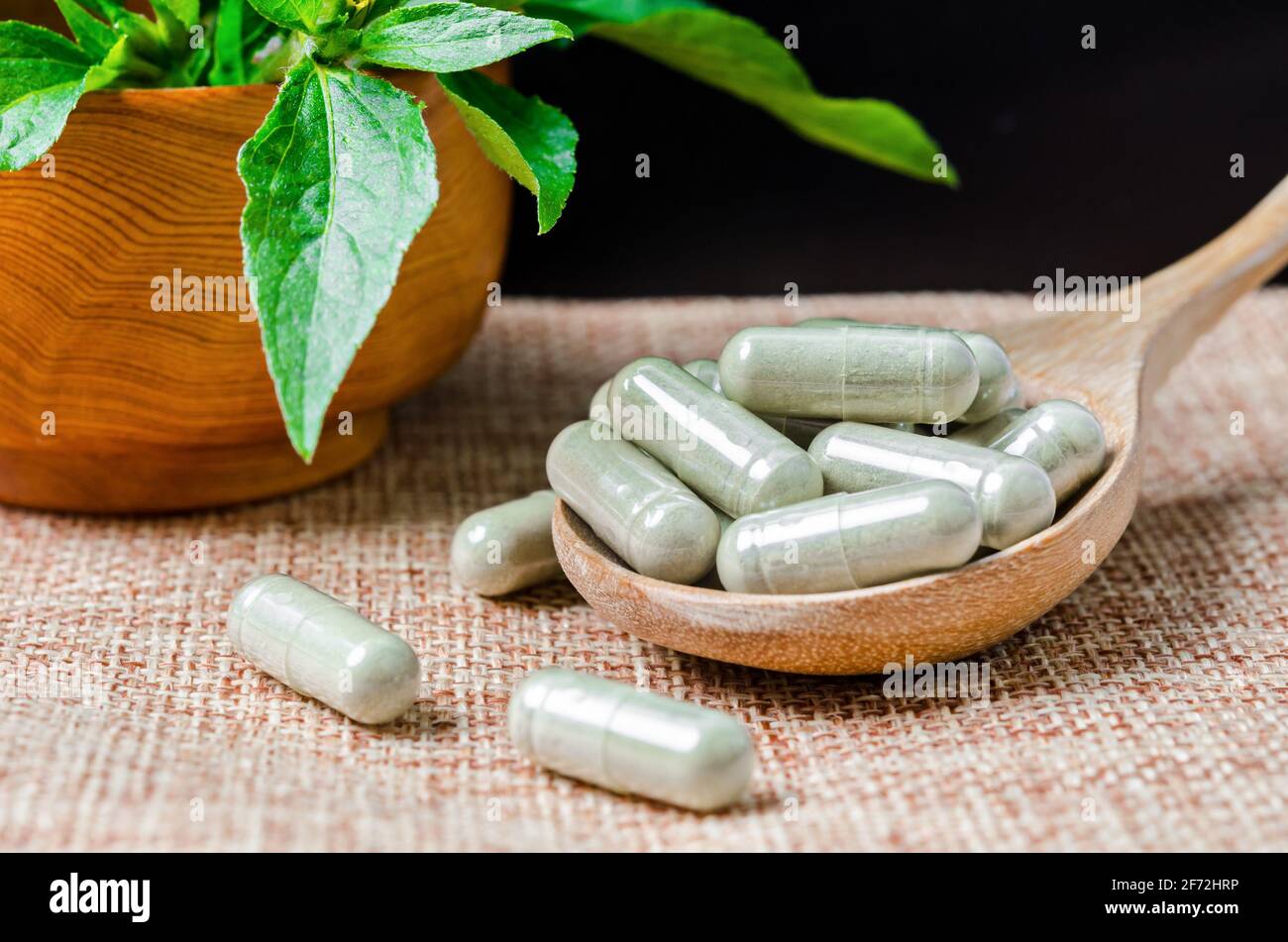 Pile of herbal medicine capsules in wooden spoon with green leaf on ...