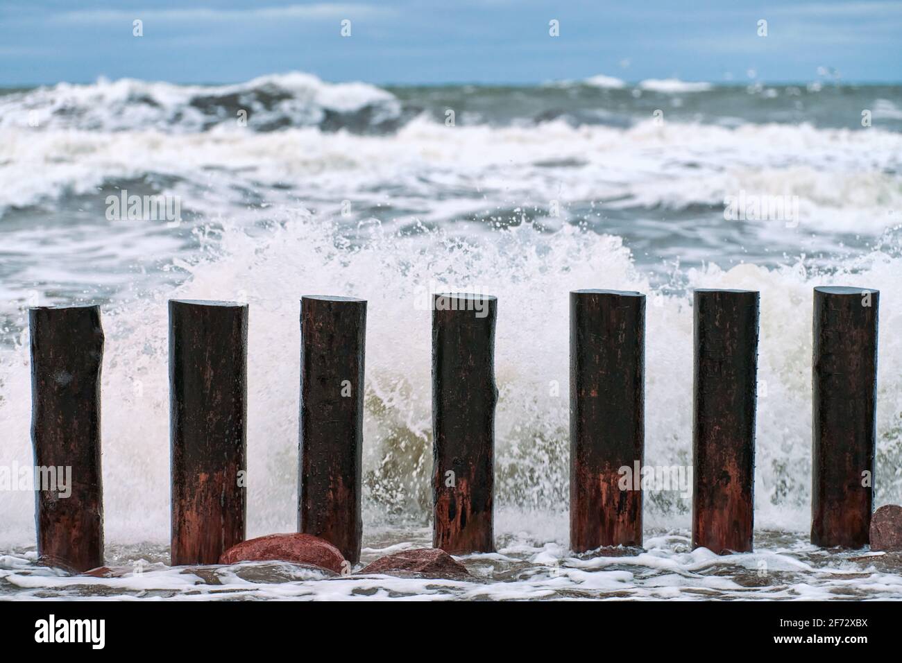 High wooden breakwaters in splashing sea waves, beautiful cloudy sky ...