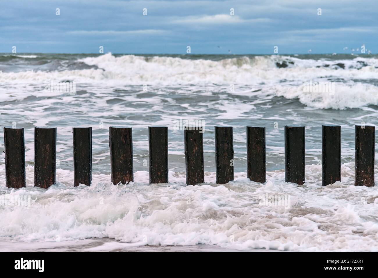 High wooden breakwaters in splashing sea waves, beautiful cloudy sky ...
