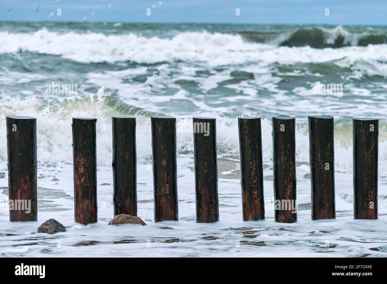 High wooden breakwaters in splashing sea waves, beautiful cloudy sky ...