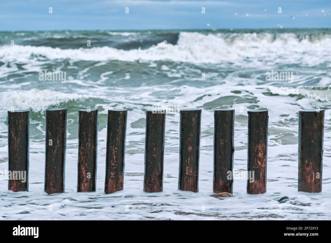 High wooden breakwaters in splashing sea waves, beautiful cloudy sky ...