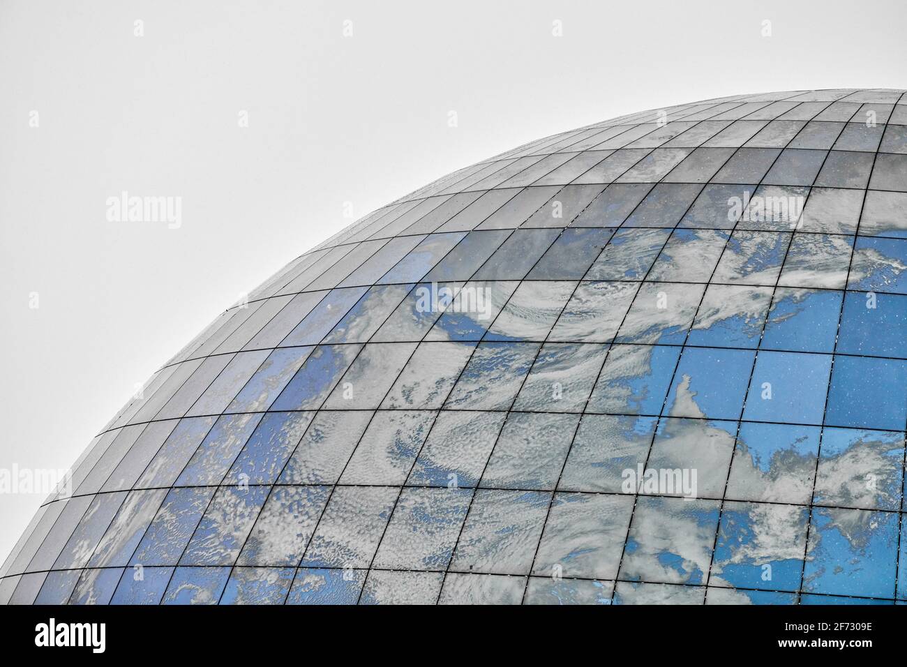 Glass spherical modern building with reflection of blue sky and clouds ...