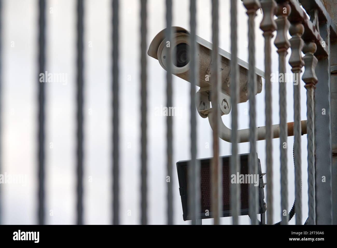 IP CCTV security camera and iron fence on grey sky background ...