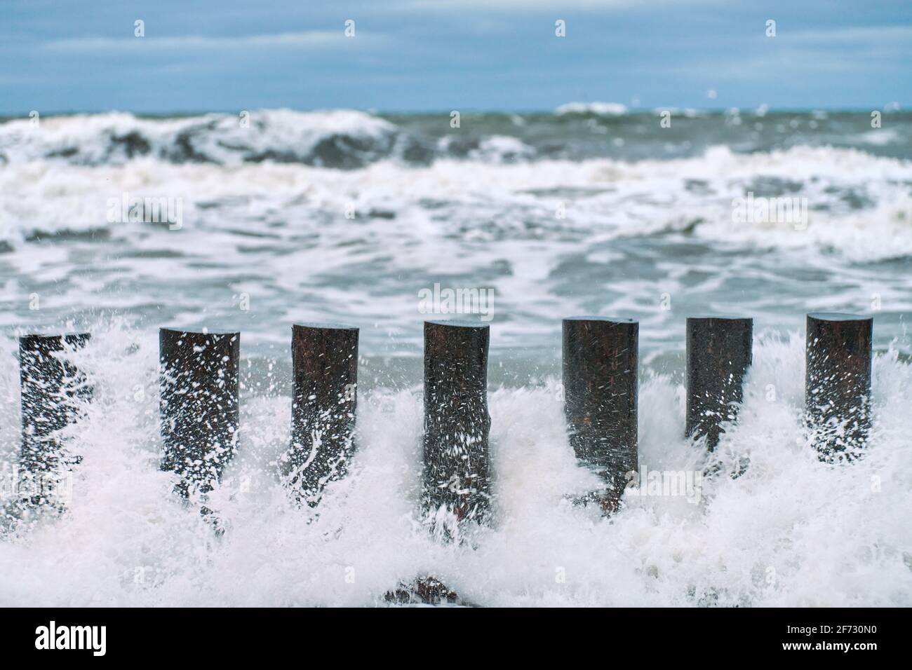 High wooden breakwaters in splashing sea waves, beautiful cloudy sky ...