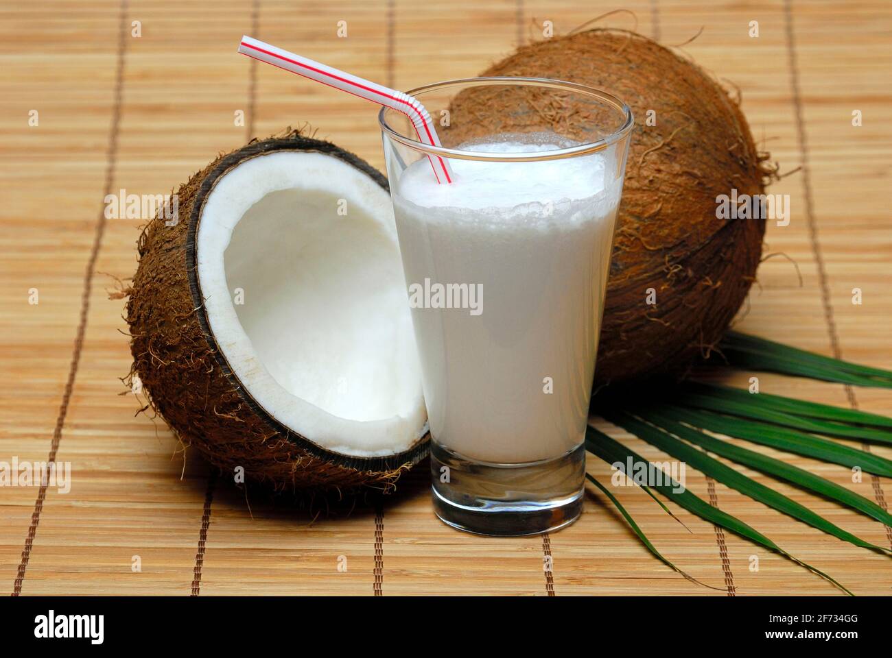 Glass of coconut milk, halved coconut, drinking straw, coconut milk ...