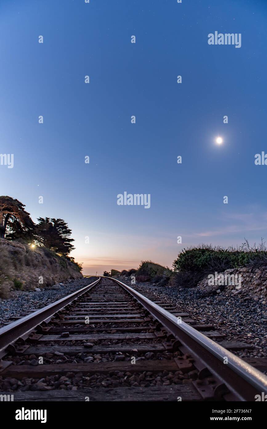 Parallel train tracks lead up to the horizon as as the bright moon and ...