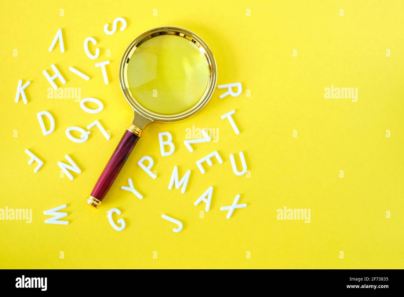 Magnifying glass on yellow background with scattered letters of ...
