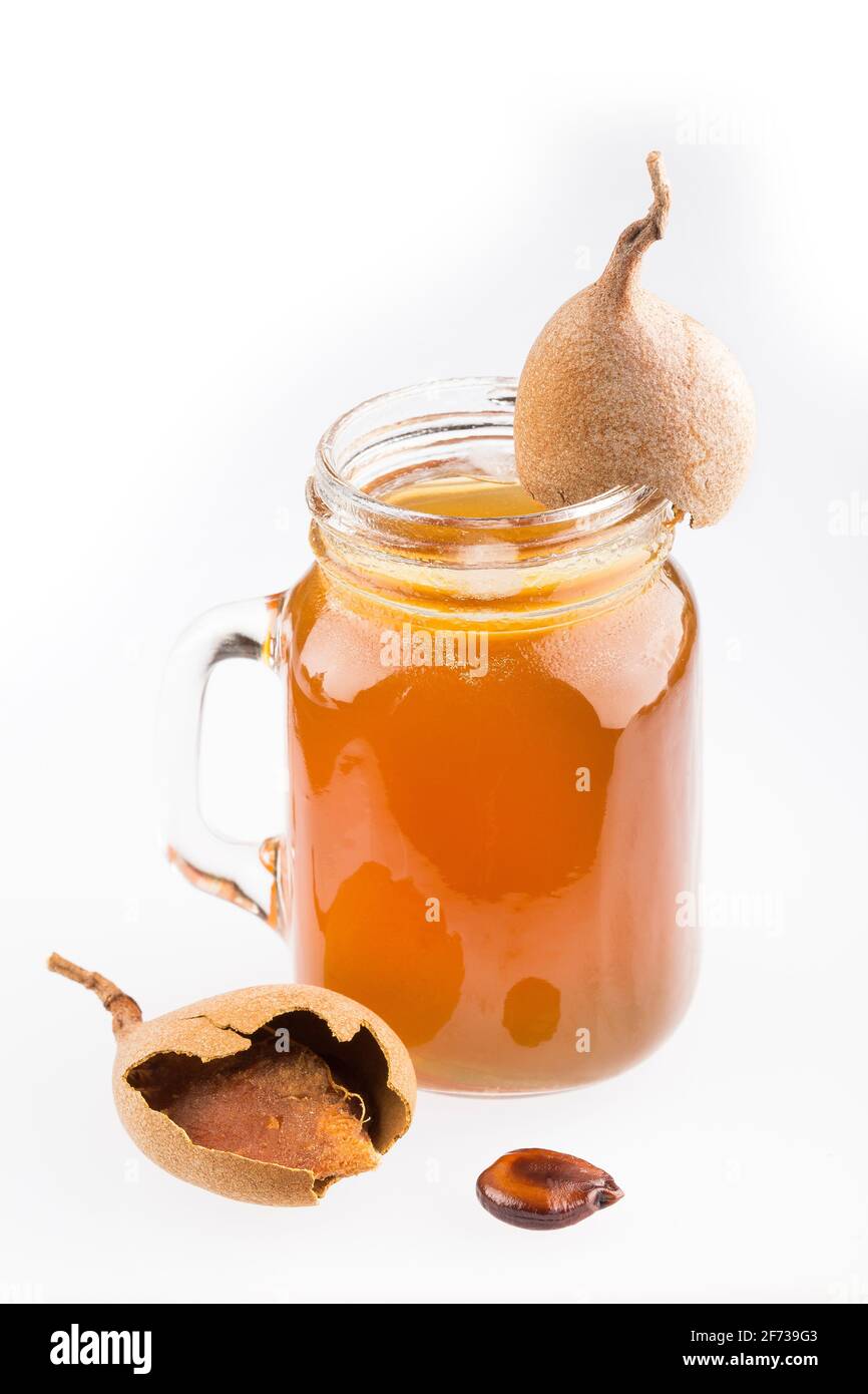 Tamarind juice in a glass surrounded by fresh ripe tamarinds ...